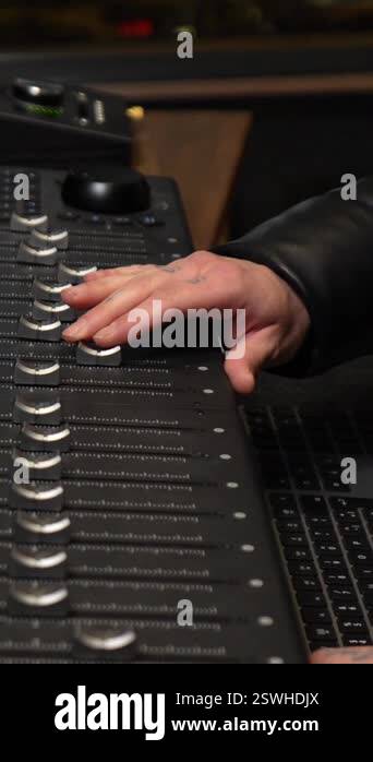 Close up of hands adjusting knobs and faders on a digital audio mixing ...