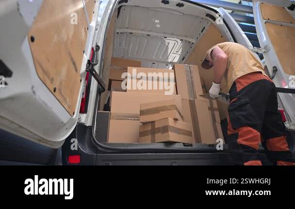 A worker organizes and unloads stacked boxes from the back of a ...