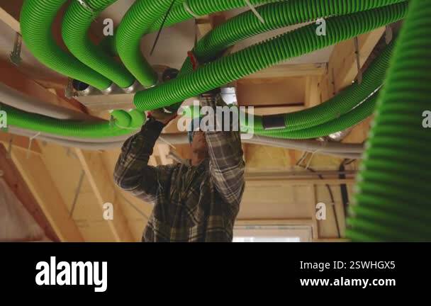 A skilled worker installs ventilation ducts on the ceiling of a construction site. Wearing ...