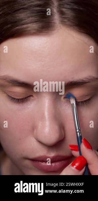 Close-up of a makeup process where vibrant blue eyeshadow is carefully ...