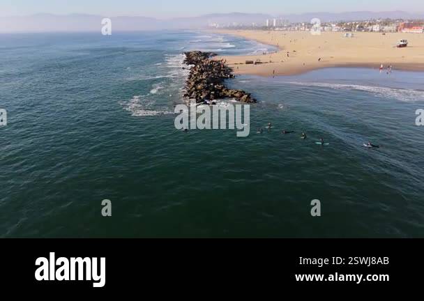 A group of surfers patiently waiting in the Pacific Ocean near a rocky ...