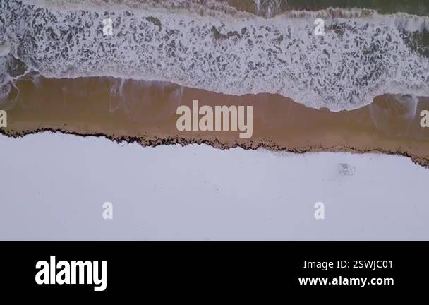 A breathtaking aerial view of ocean waves crashing onto a snow-covered ...