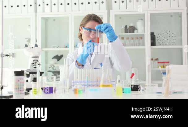 Female scientist examines test tube containing red liquid in laboratory ...