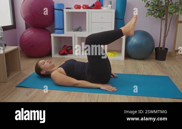 Woman exercising on yoga mat in gym surrounded by equipment like ...