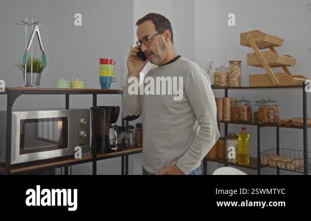 Hispanic man talking on phone in an office kitchen surrounded by ...
