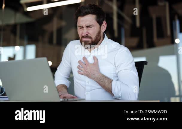 Stressed businessman experiencing chest pain in office. Exhausted male ...