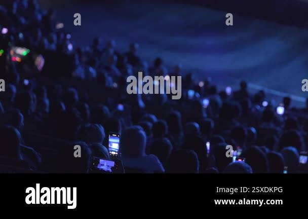 A crowded theater audience filming a live stage event with smartphones ...