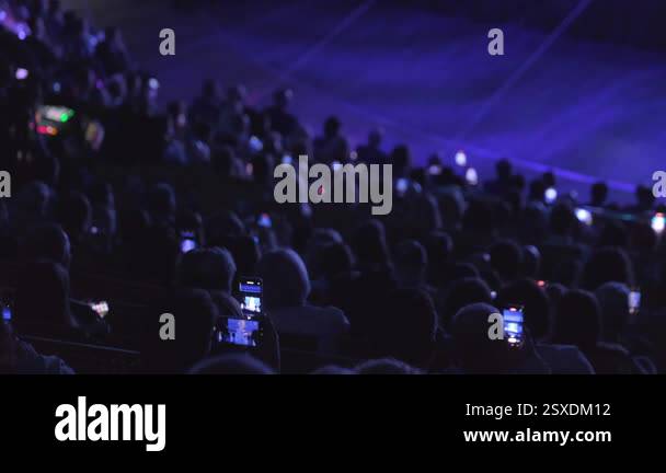 Crowd members watch a performance while recording with smartphones ...