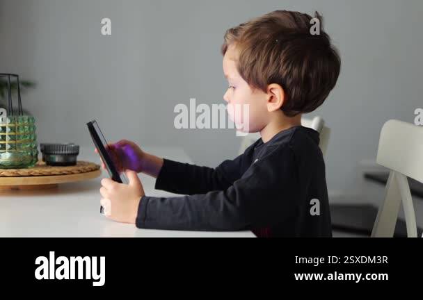 Curious little boy touches screen of tablet with finger searching game ...
