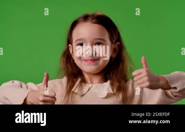 Children emotions concept. Little girl child looks at camera and shows thumb up hand sign ...