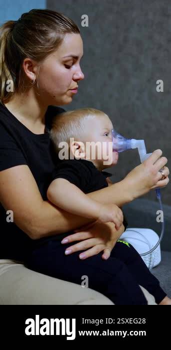 A little boy sits on the couch and breathes with an inhaler ...