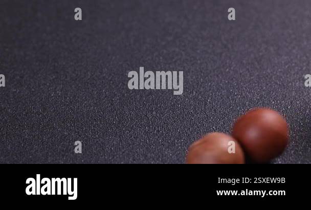 Macadamia nuts bouncing and rolling across dark textured surface ...