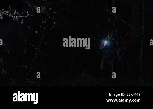 A lost man walks through a dark forest at night, holding a flashlight ...