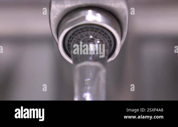 Water flows from sleek chrome-plated faucet, shifting focus from ...