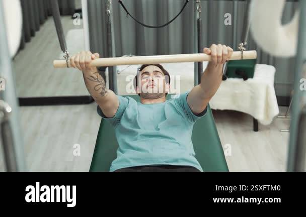 Man performing seated core exercise on pilates trapeze holding bar to ...
