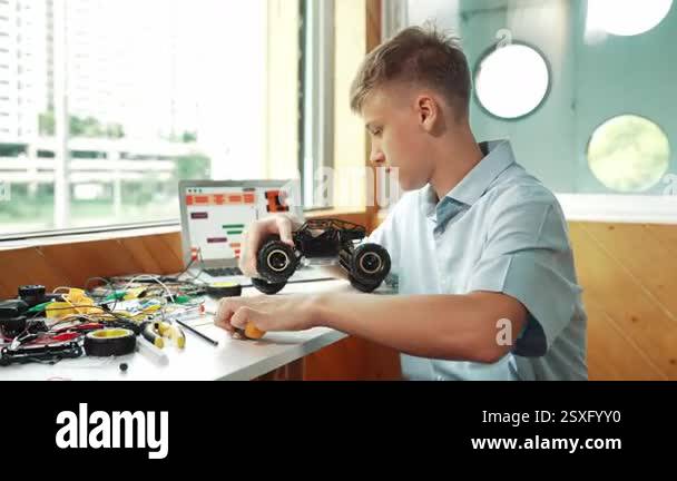 Happy teenager fixing robotic model while using electronic equipment ...