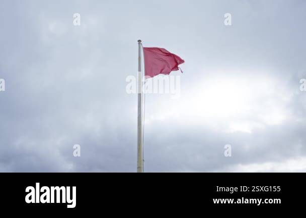 Red flag waving on a pole against a cloudy sky during daylight in an ...