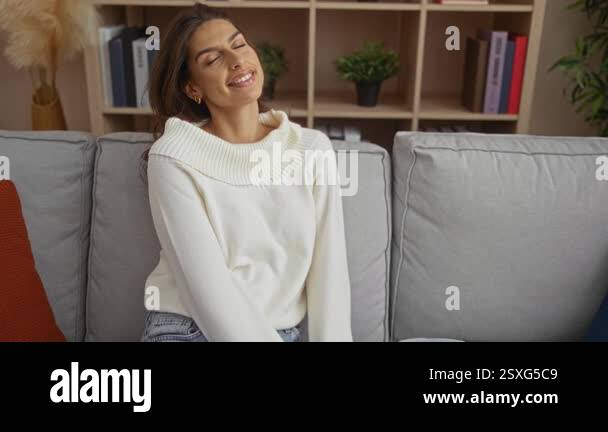 Woman smiling sitting on a gray sofa in an apartment living room ...