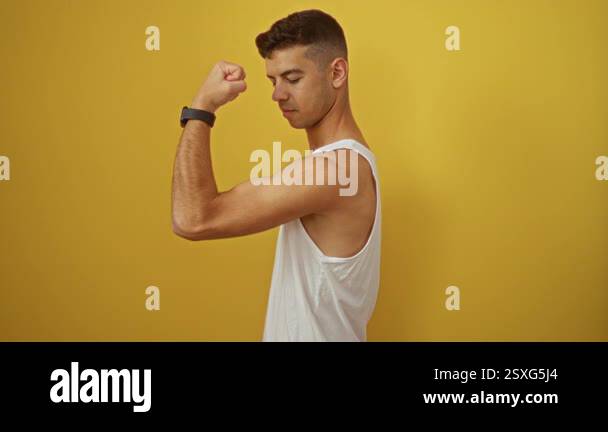 Young man flexing arm muscles confidently against a bright yellow ...