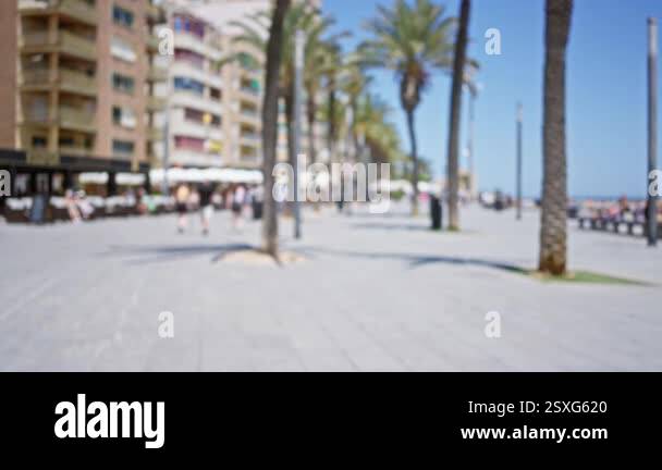 Defocused view of people walking along an outdoor promenade with palm ...
