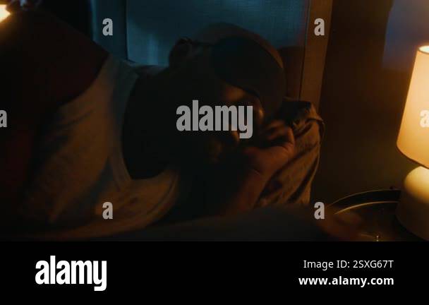 African American man, wearing sleep mask, turning off his bedside table ...