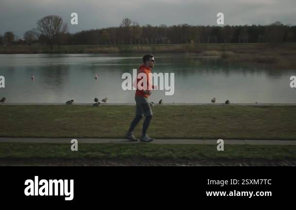 Sporty man jogging along footpath along lake in park in Germany, Munich ...