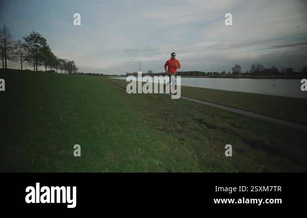 Sporty man jogging along footpath along lake in park in Germany, Munich ...