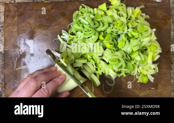 Chef chops leek stems with a cleaver on wooden cutting board Stock ...