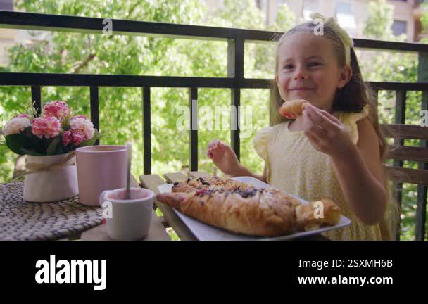 Close-up shot of happy, cute child eating crusty pastry with fruity jam ...