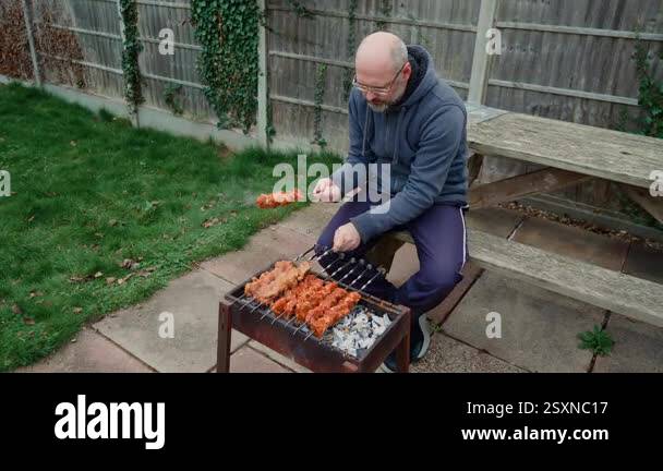 Man lifting skewer of grilled meat from barbecue on patio. Male ...