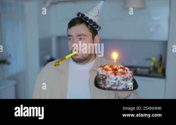 A sad, middle-aged man wearing a party hat and whistling in a festive ...
