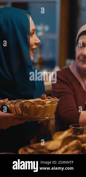 Vertical Screen: Cheerful woman in a blue hijab shares bread at a warm ...