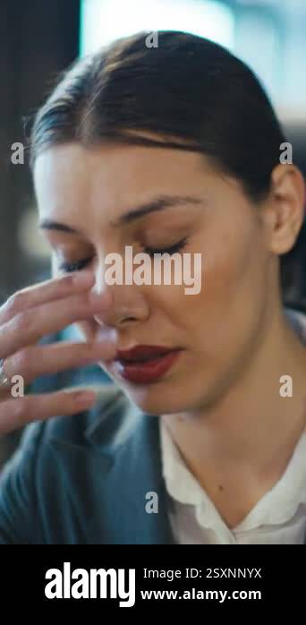 Vertical: Stressed businesswoman in a modern office rubs her forehead ...