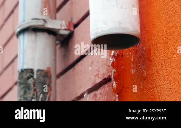 Water drips from a pipe onto a vibrant orange wall in a rainy setting ...