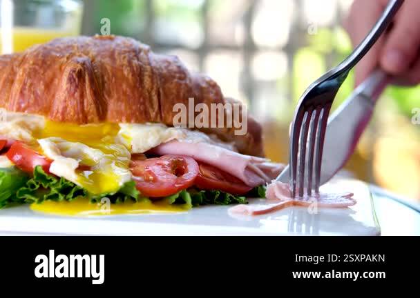 Croissant sandwich with Serrano ham and arugula leaves, hands placing ...