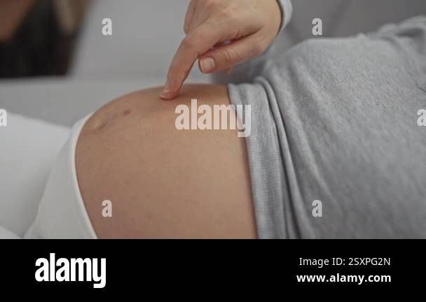 Pregnant woman gently touching her belly in a cozy home setting ...