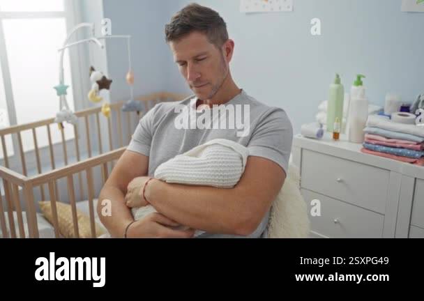 Man cradles baby in cozy bedroom, sitting beside crib, embodying ...