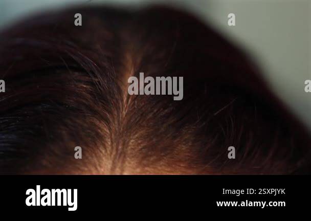 woman with oily hair lowers her head, hair roots visible up close ...