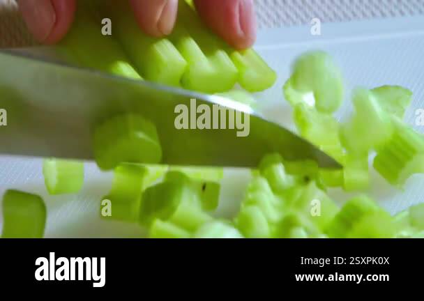 Close-up. A chef is slicing celery stalks on a white kitchen board ...