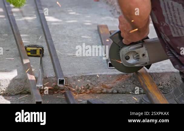 man cutting square steel pipes with angle grinder on concrete edge ...