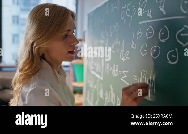 School teacher solving math equations on blackboard with chalk closeup. Focused woman writing ...