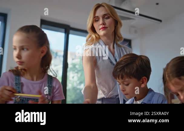 Woman teacher guiding art lesson in primary school. Young lady helping pupils in creative work ...