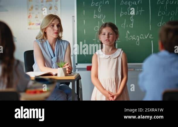 Elementary schoolgirl answering lesson standing near teacher table ...