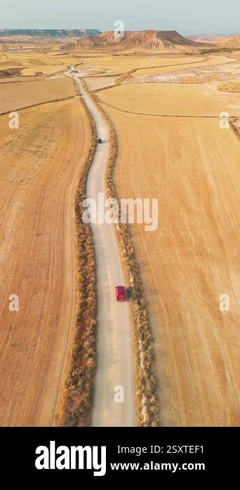 Red car driving through the mountainous desert landscape of Bardenas ...