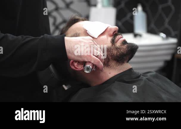 Professional barber carefully shaving a relaxed clients beard with an ...