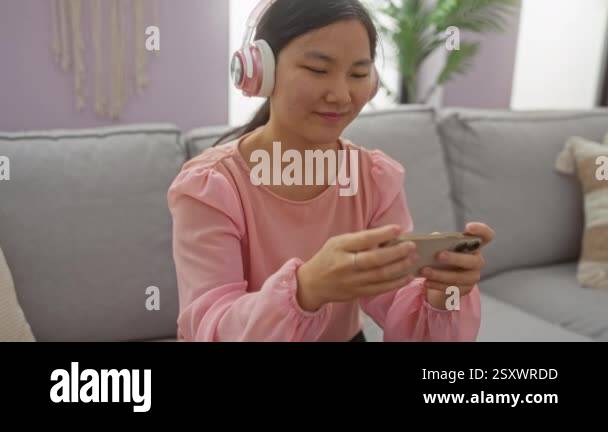 Woman playing a mobile game seated on a comfortable gray sofa wearing ...