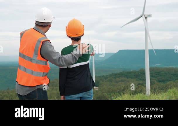 Engineer with his son on a wind farm atop a hill or mountain in the ...