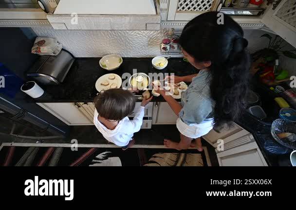 In a bright kitchen, Oksana Eney guides a young child through the ...