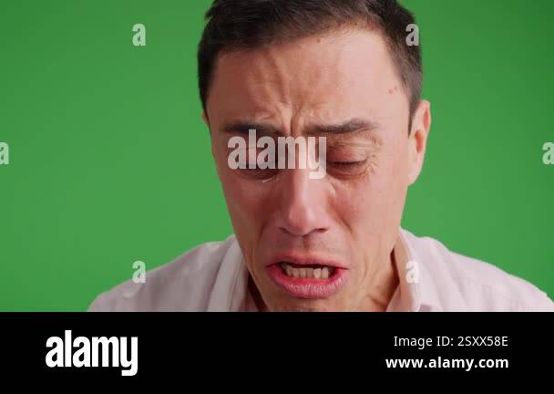 Close up of a sad man crying desperately looking at camera, on a green ...