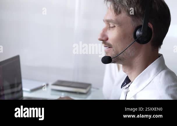 Happy smiling male call center operator in white casual shirt is assisting clients online ...